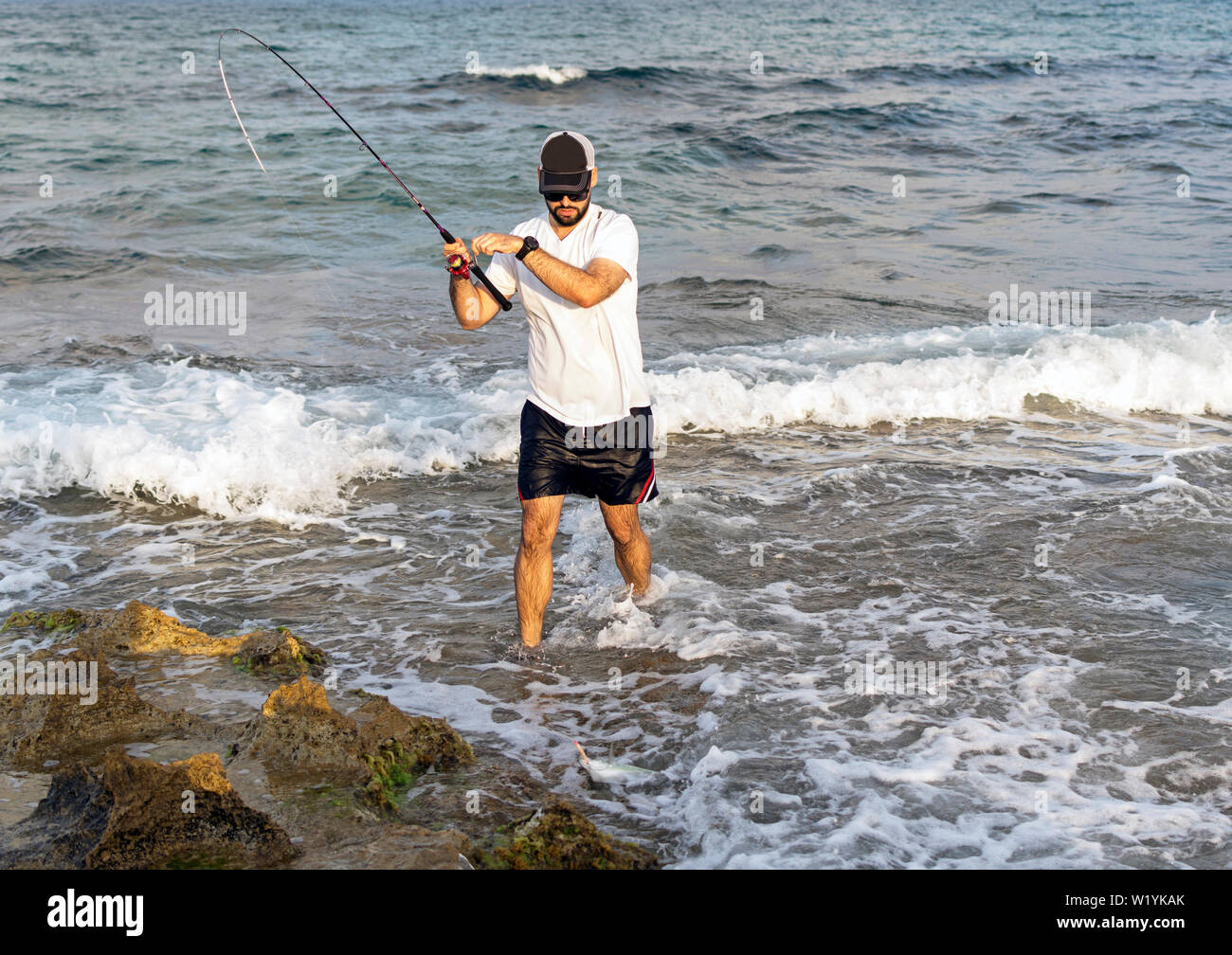 Fisherman standing at seashore hooks a fish. Sportsman holds a fishing ...