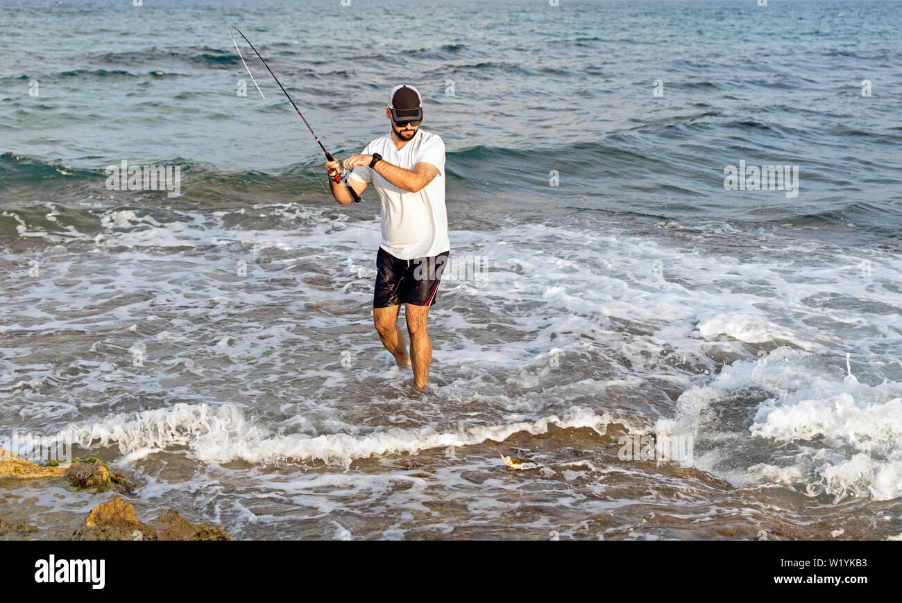 Fisherman standing at seashore hooks a fish. Sportsman holds a fishing ...