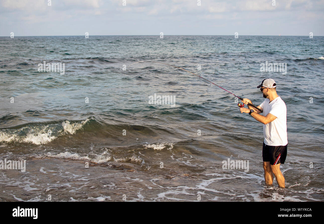 Fisherman standing at seashore hooks a fish. Sportsman holds a fishing ...
