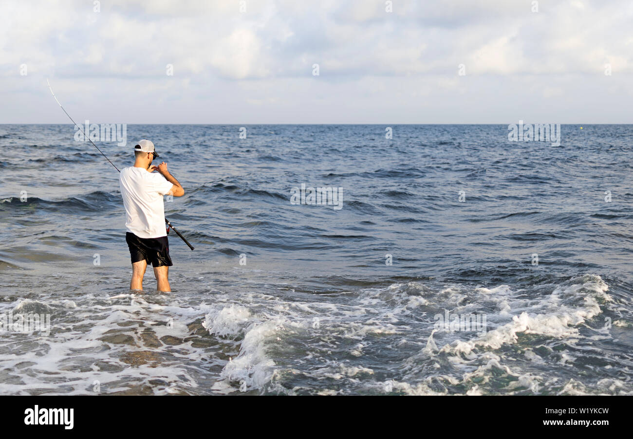 Fisherman standing at seashore hooks a fish. Sportsman holds a fishing ...