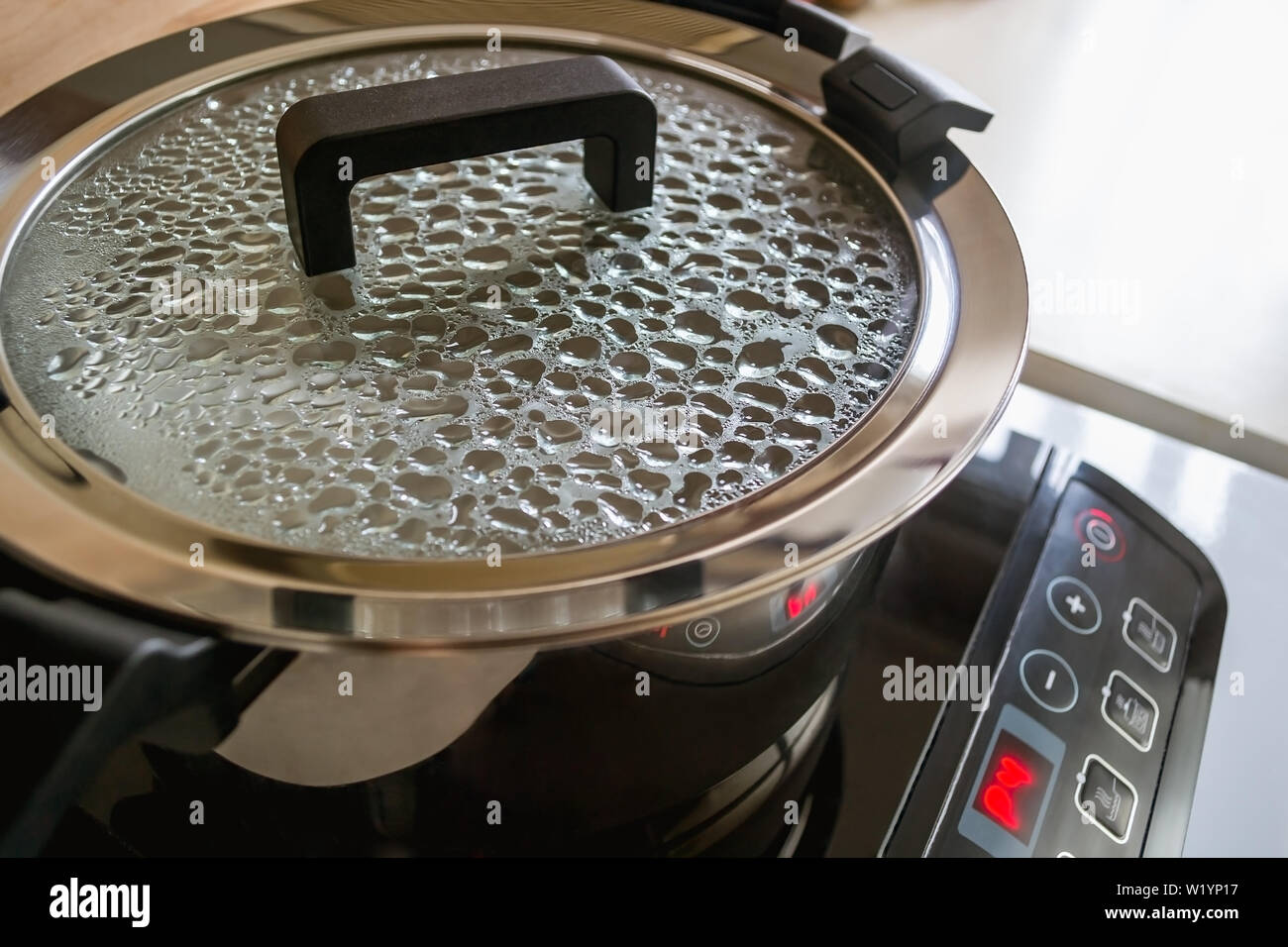 Modern metal soup pan with black handles on an induction stove. Drops ...
