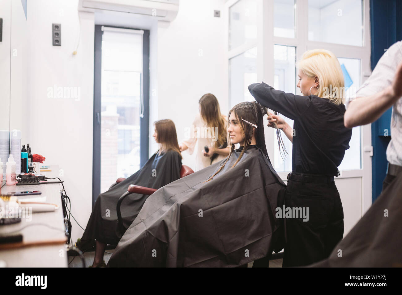 hairdresser holding scissors and comb and makes haircut woman client ...