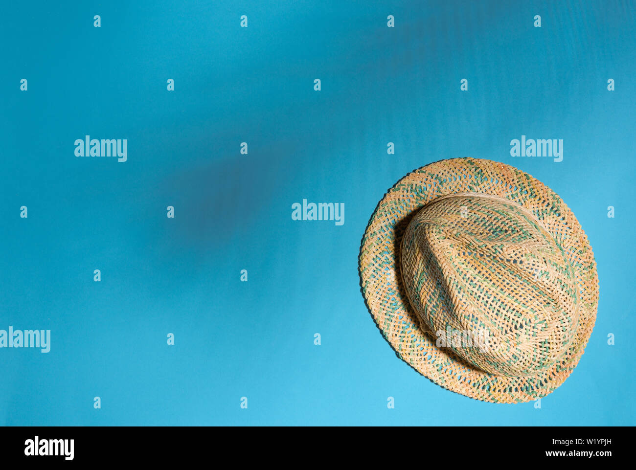 Straw hat and strong shadow of tropical palm leaves on blue background ...