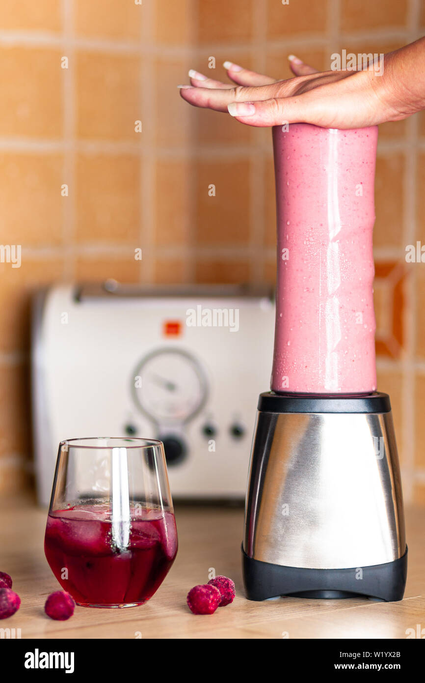 Woman hand blending fruit shake on the kitchen table with cherries ...