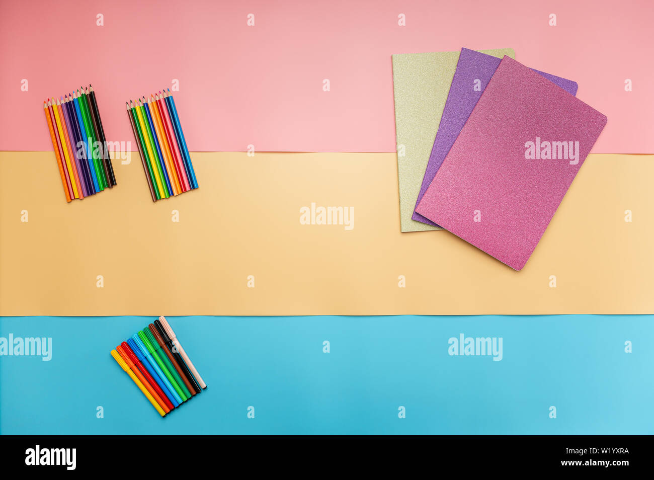 Shiny notebooks, colour pencils and colouring pens on a colourful paper ...