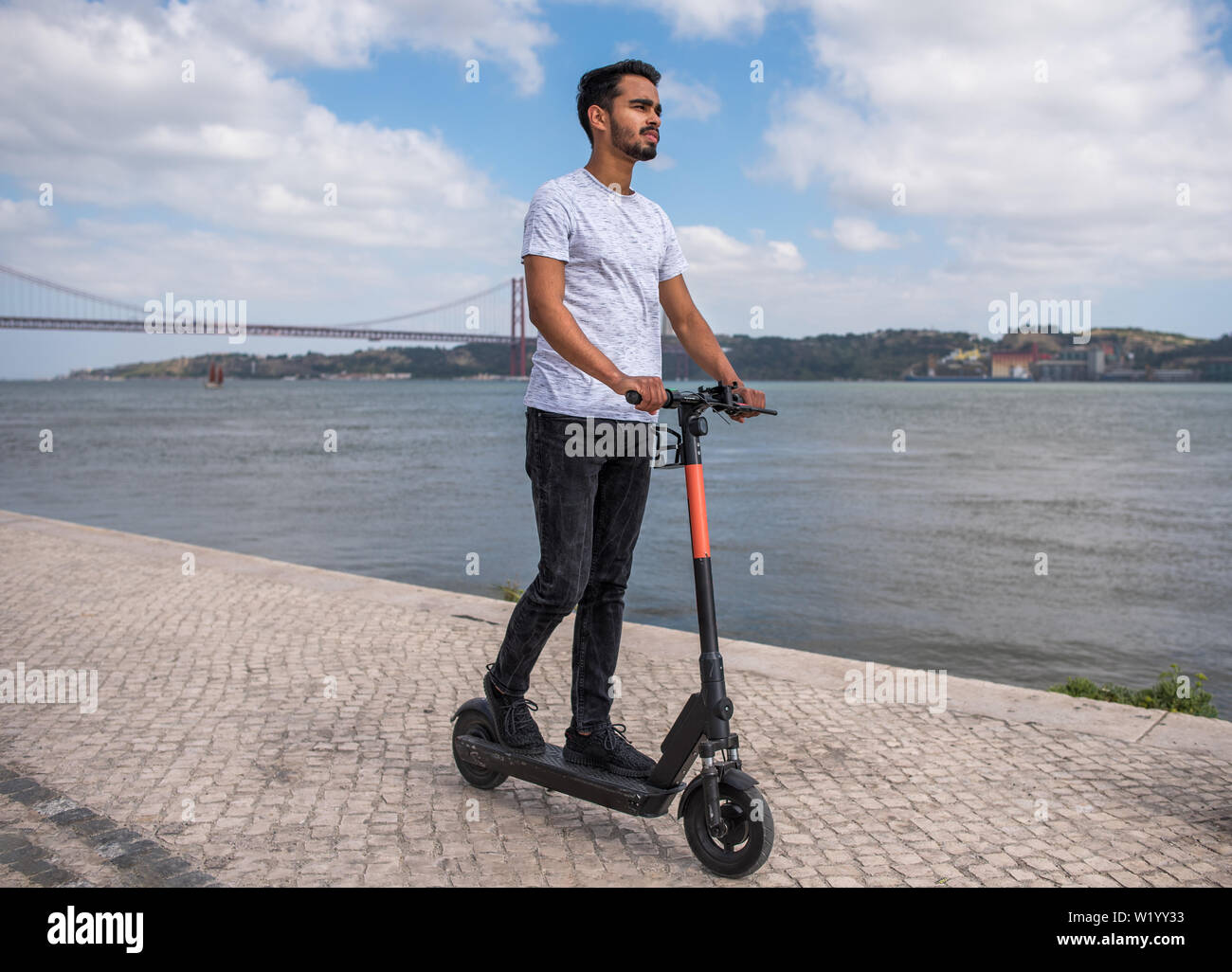 young male model riding a scooter in front of river Tejo in Lisbon ...