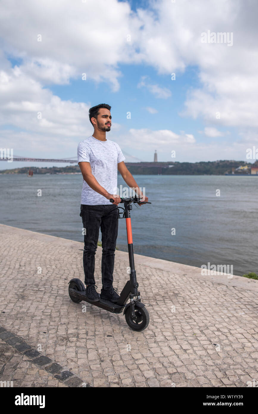 young male model riding a scooter in front of river Tejo in Lisbon ...