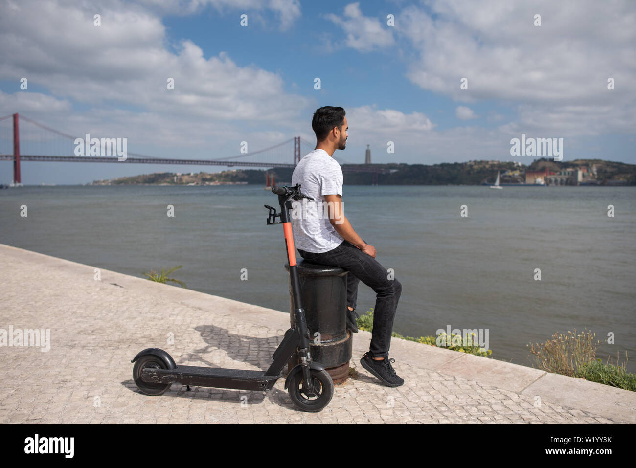 young male model sitting in front of river Tejo in Lisbon with a ...