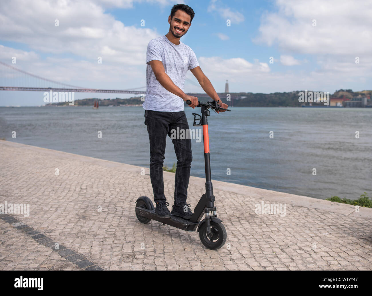 young male model riding a scooter in front of river Tejo in Lisbon ...
