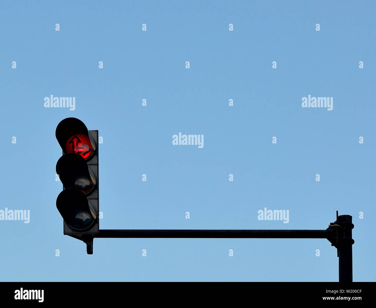 Red traffic light installed on a pole above a roadway, against a blue ...