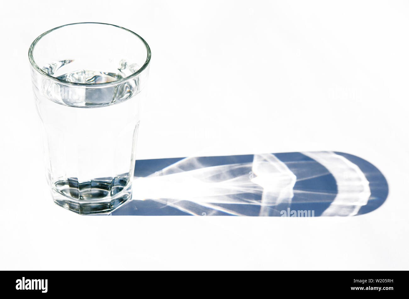 Glass beaker from which padajet sharp shadow, stands on a white ...