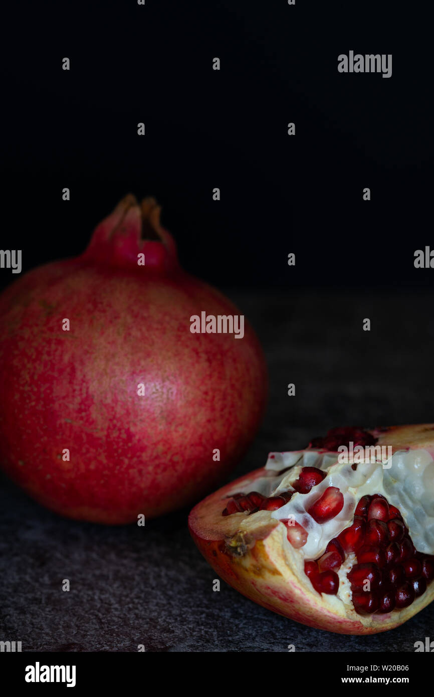One whole pomegranate (Punica granatum) and one cut piece with vibrant ...