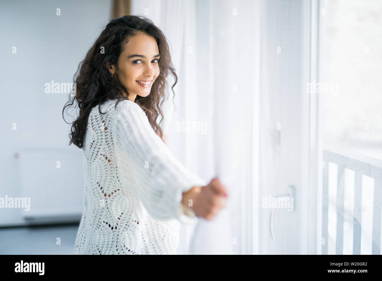 Beautiful woman opening curtains and looking through the window Stock ...
