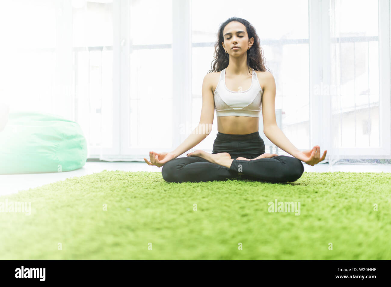 Attractive young woman exercising and sitting in yoga lotus position ...