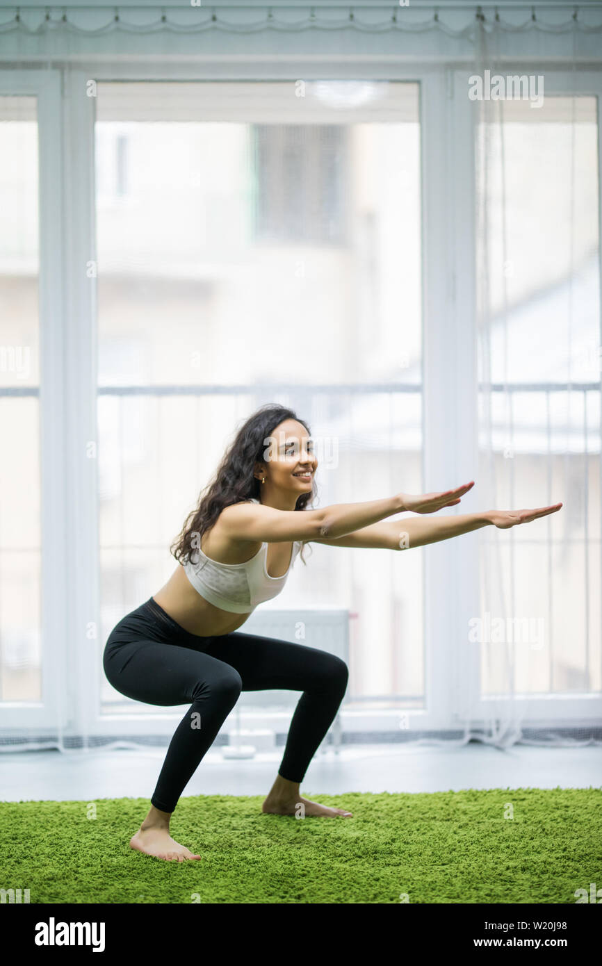 Side view of young woman doing squats on exercise mat in a living room ...