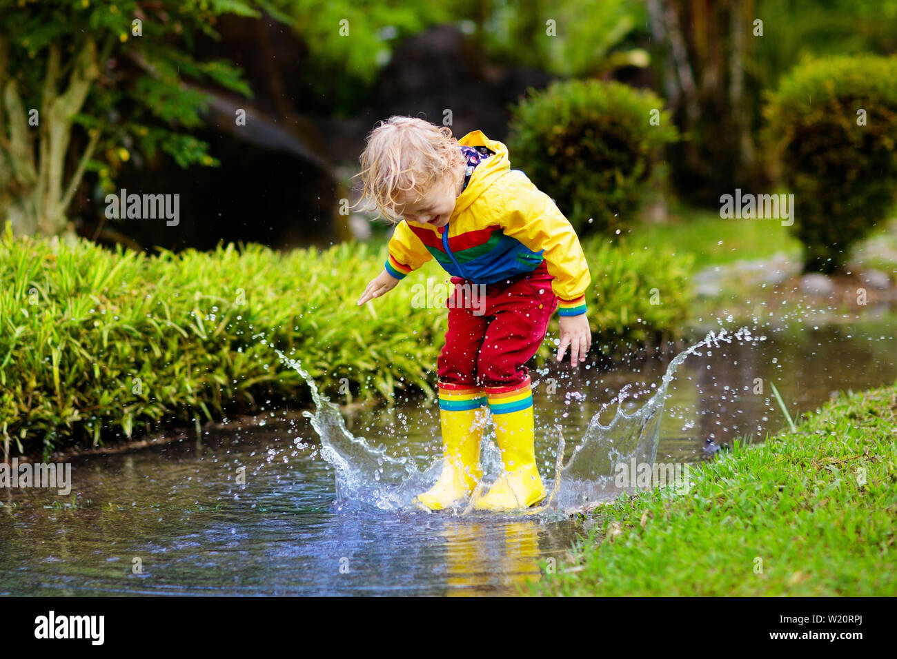 Child playing in puddle. Kids play and jump outdoor by autumn rain ...
