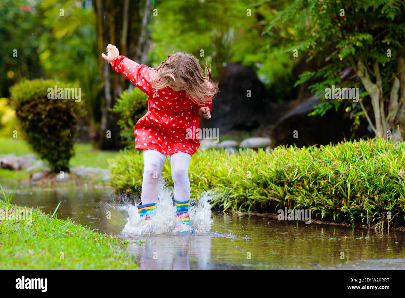 Child playing in puddle. Kids play and jump outdoor by autumn rain ...