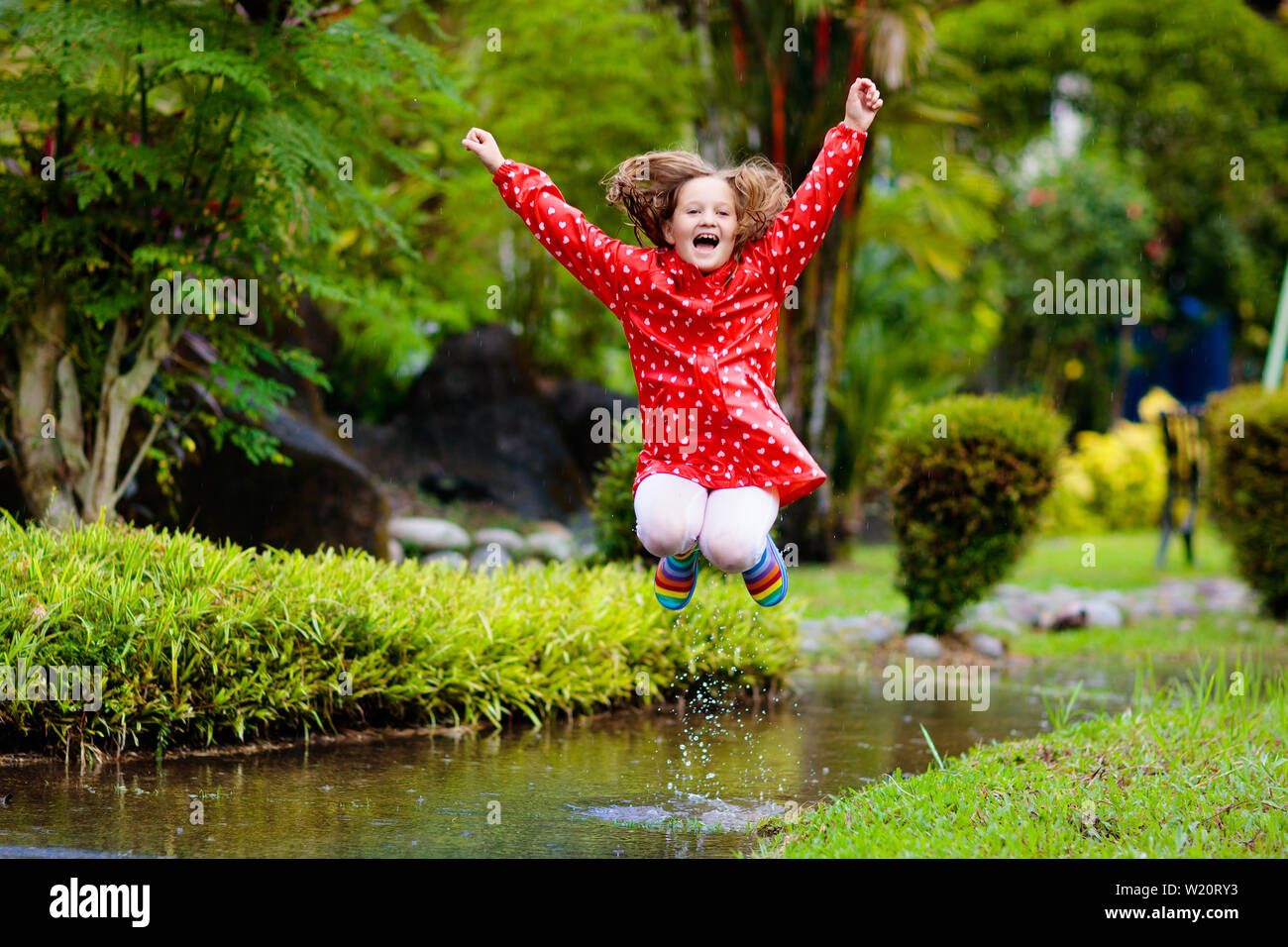 Child playing in puddle. Kids play and jump outdoor by autumn rain ...