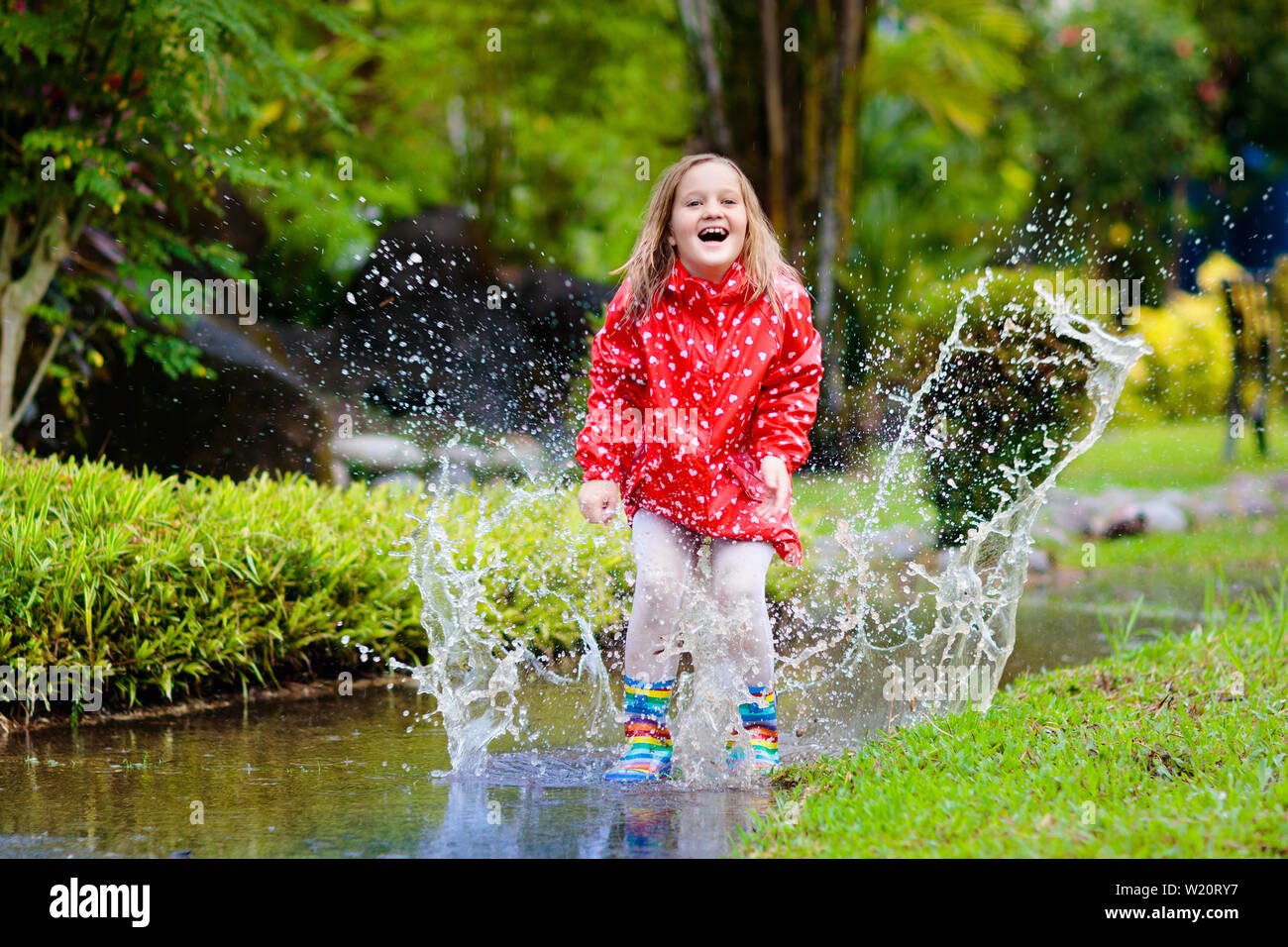 Child playing in puddle. Kids play and jump outdoor by autumn rain ...