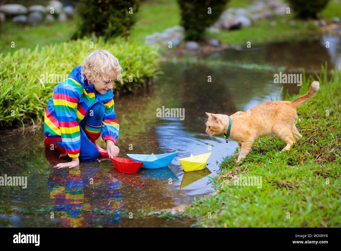 Child and cat playing with paper boat in puddle. Kids play outdoor by ...