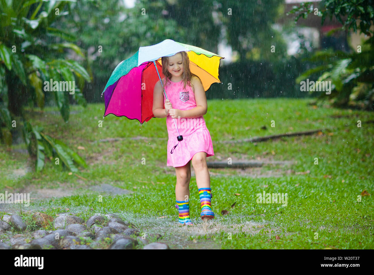 Kid playing out in the rain. Children with umbrella and rain boots play ...