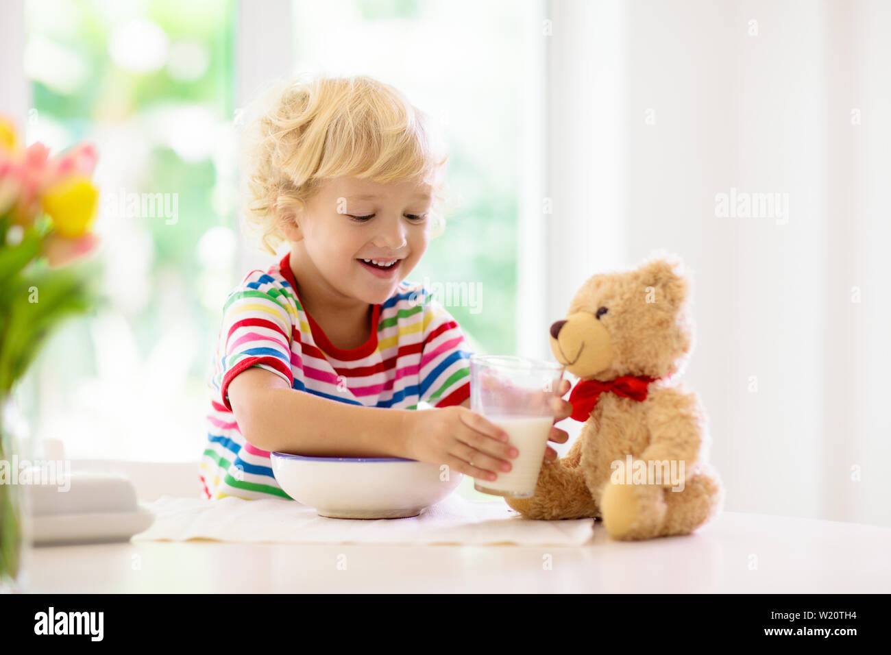 Child having breakfast. Kid feeding teddy bear toy, drinking milk and ...