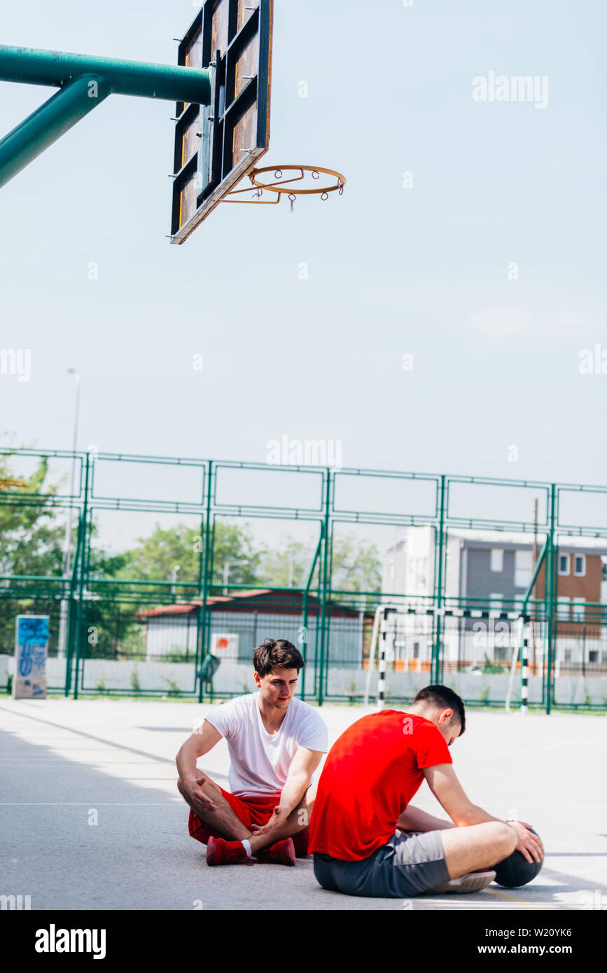 Two strong caucasian athletes resting on the ground at the basketball ...