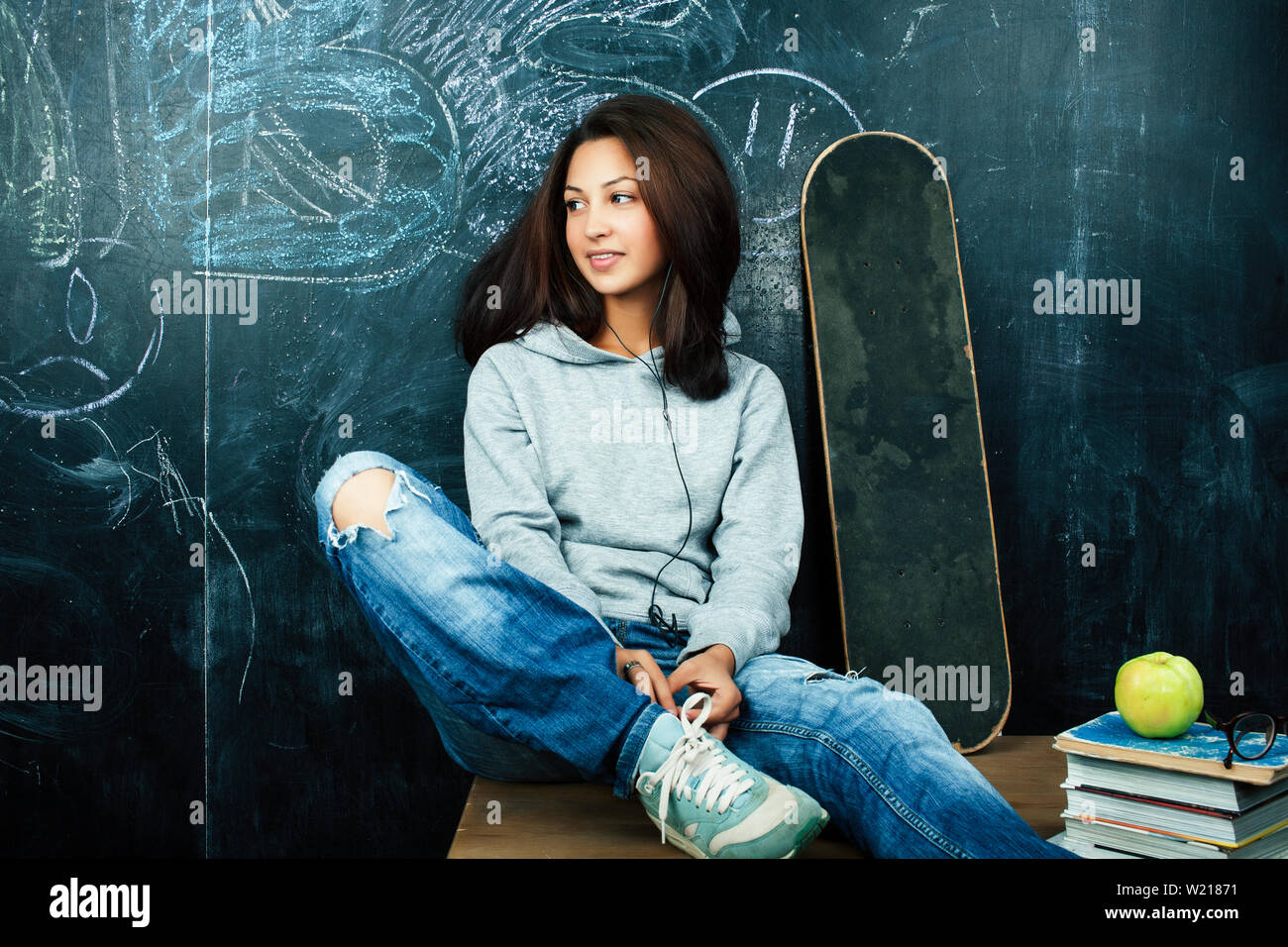 young cute teenage girl in classroom at blackboard seating on table ...
