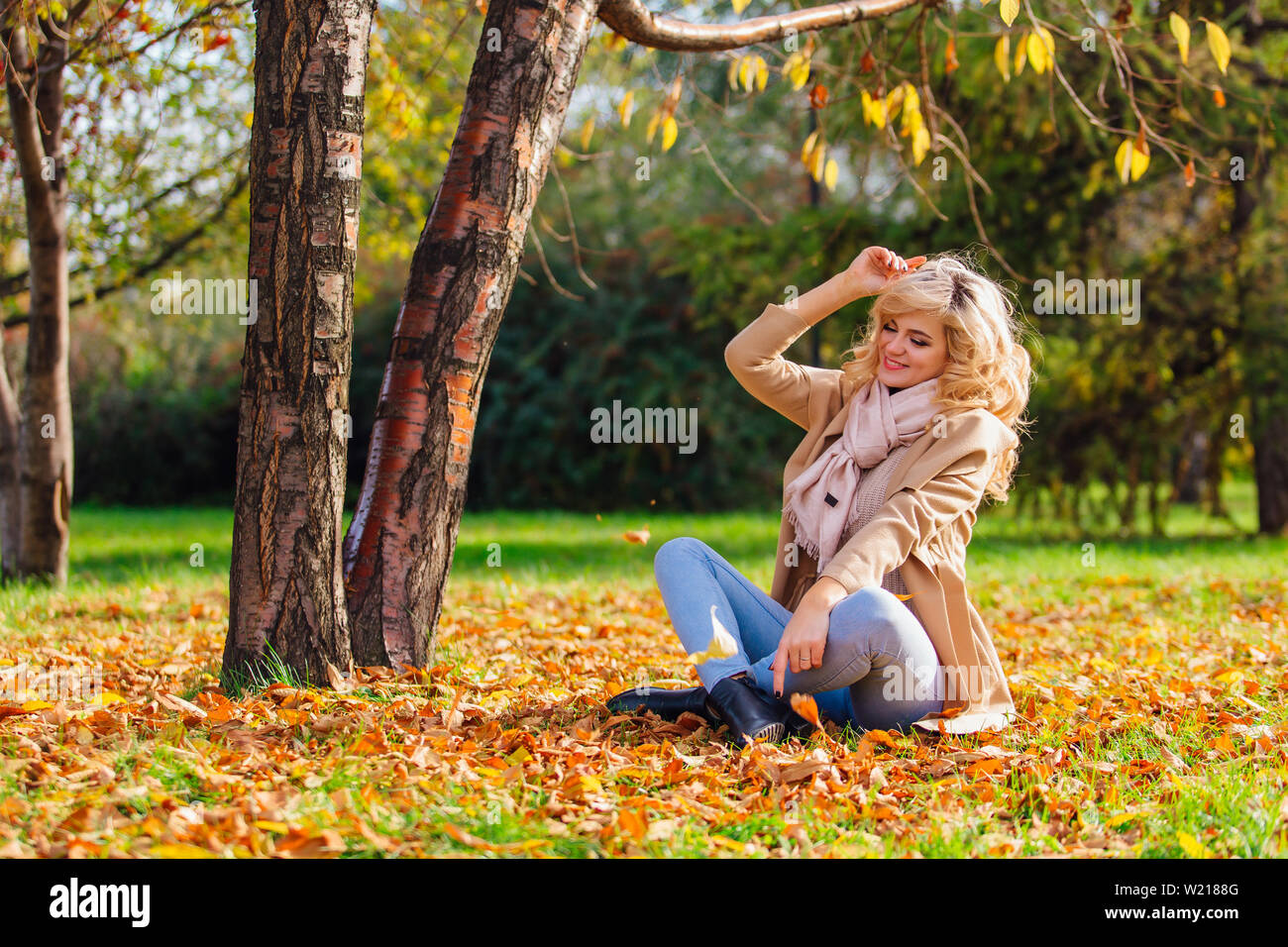 Young beautiful woman sitting under the tree on the ground coverd with ...