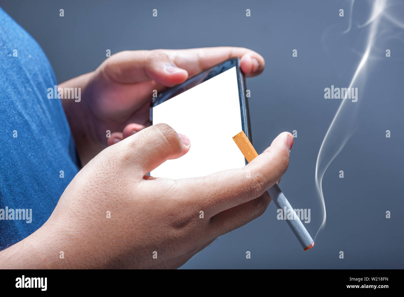 Man smoking cigarette while holding mobile phone on gray background ...