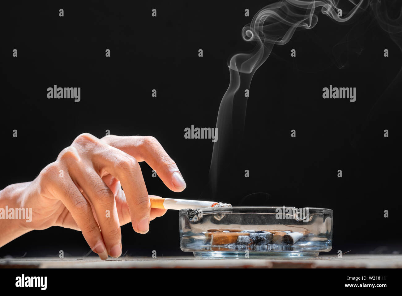 Hand holding a cigarette on wooden table with transparent ashtray and ...