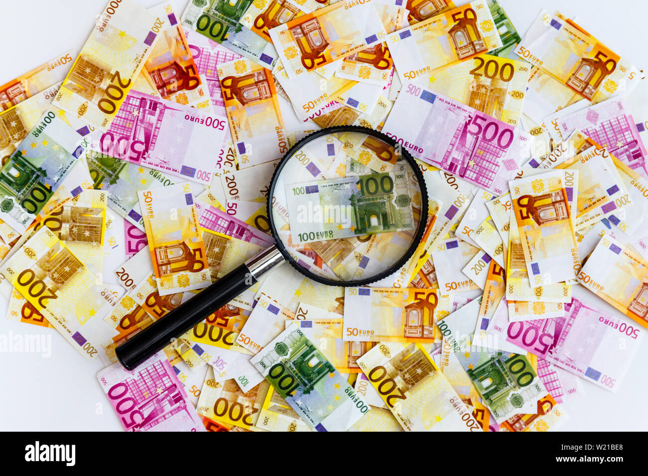 a lot of euro banknotes on a white background and a magnifying glass on ...