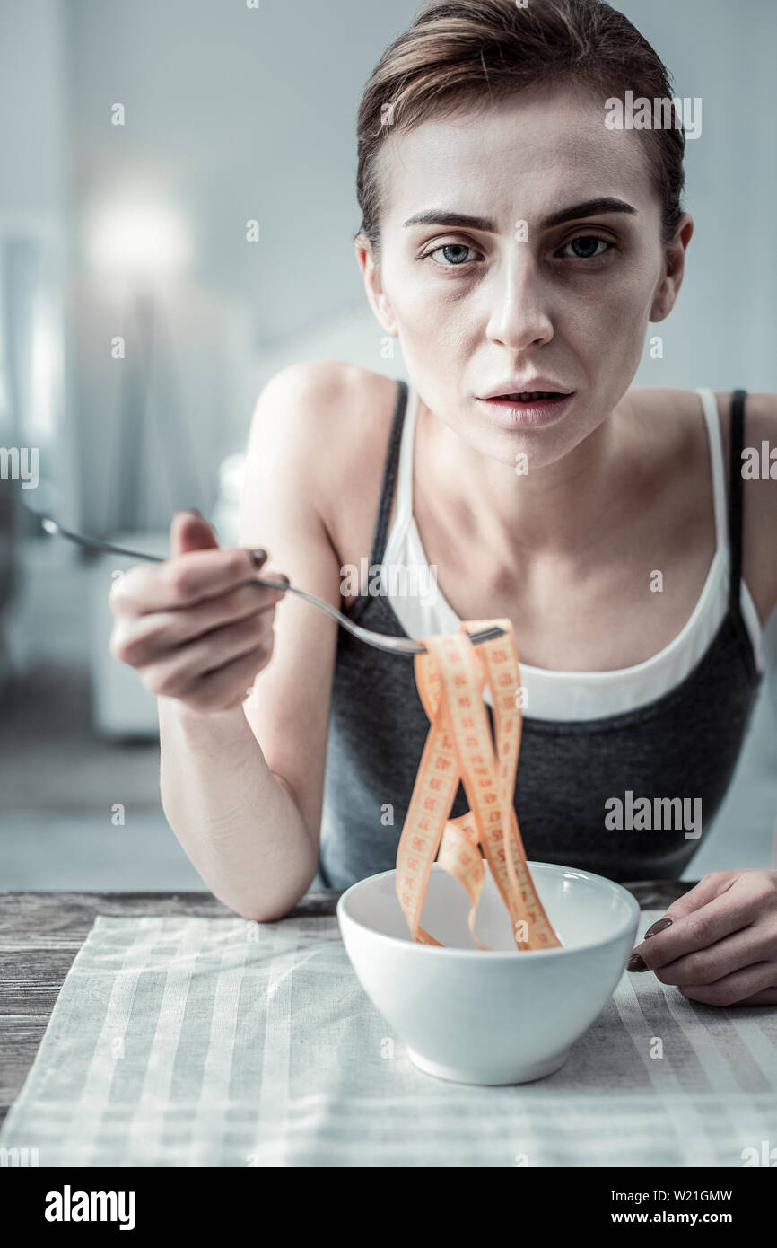 Join me. Anorexic girl sitting at the table and dreaming about fat ...
