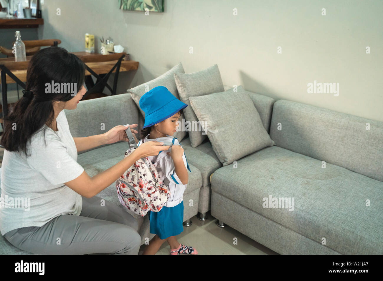 mom help her little girl to put a backpack on before going to school ...