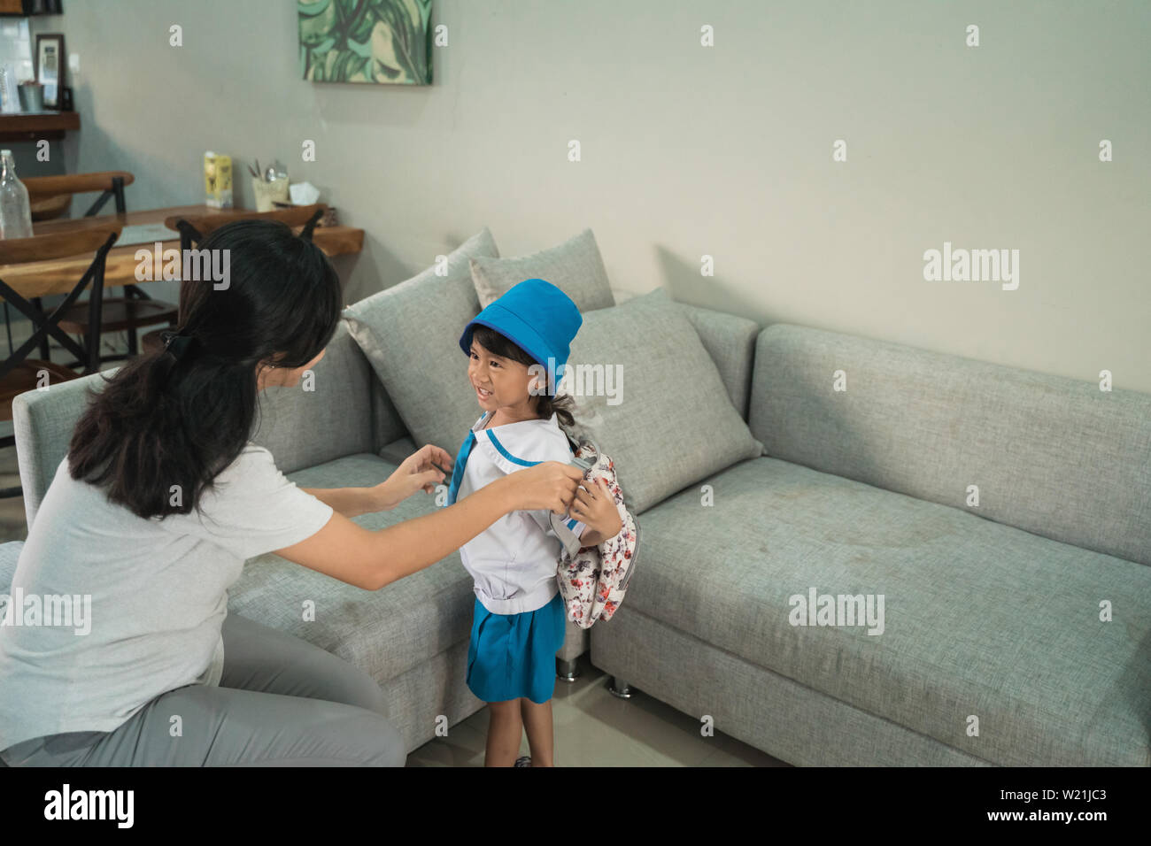 mom help her little girl to put a backpack on before going to school ...