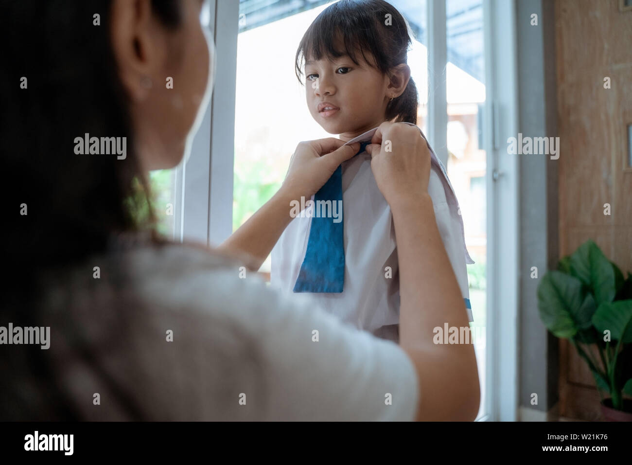 mom help to put on uniform on her daughter in the morning before going ...