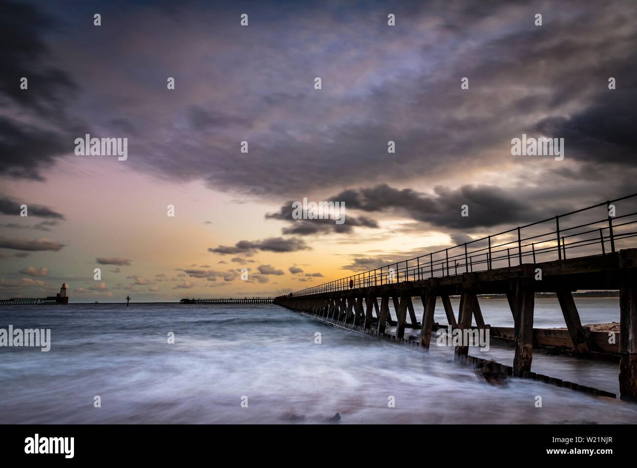 Bridge in the sea with dramatic clouds at sunset, harbour entrance ...