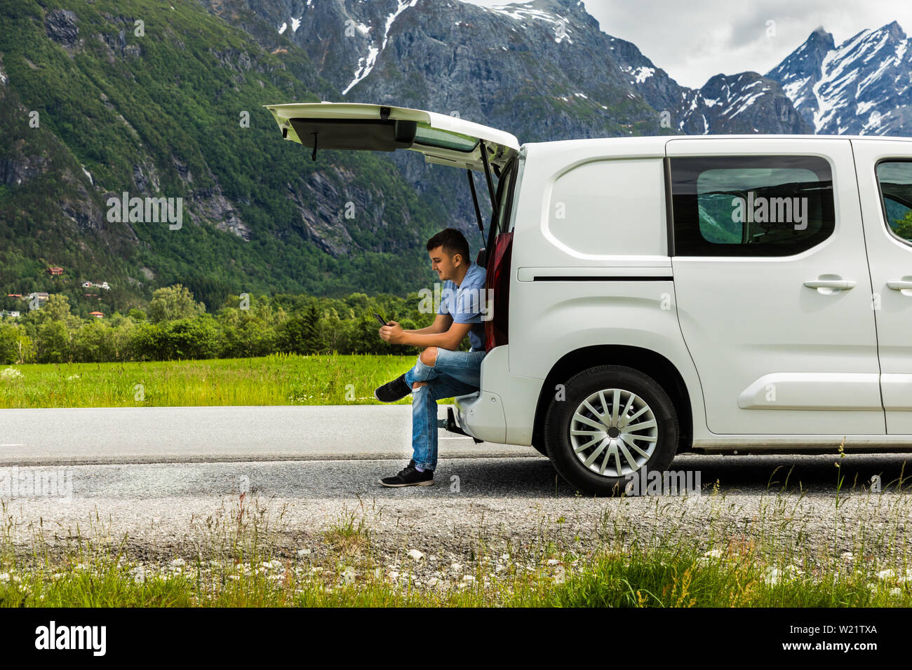 Young man sitting in the trunk of the car and use mobile phone on the ...