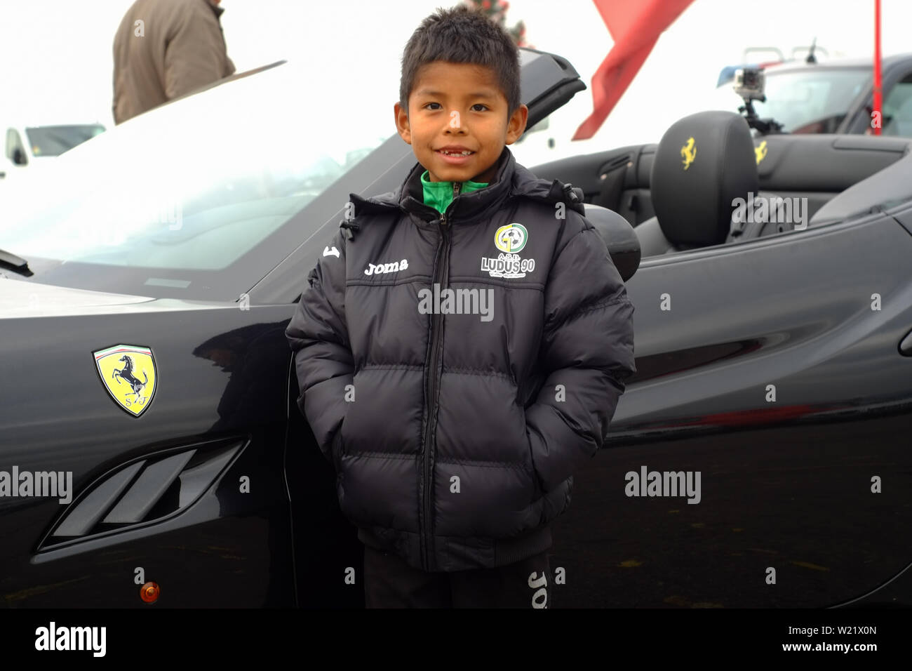 Black luxury italian Ferrari car parked with latin boy beside it. Early ...