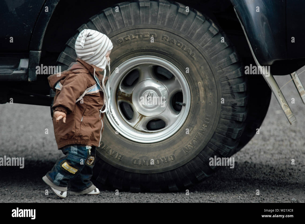 Young kid near a big foot SUV compares his tall with the giant car ...