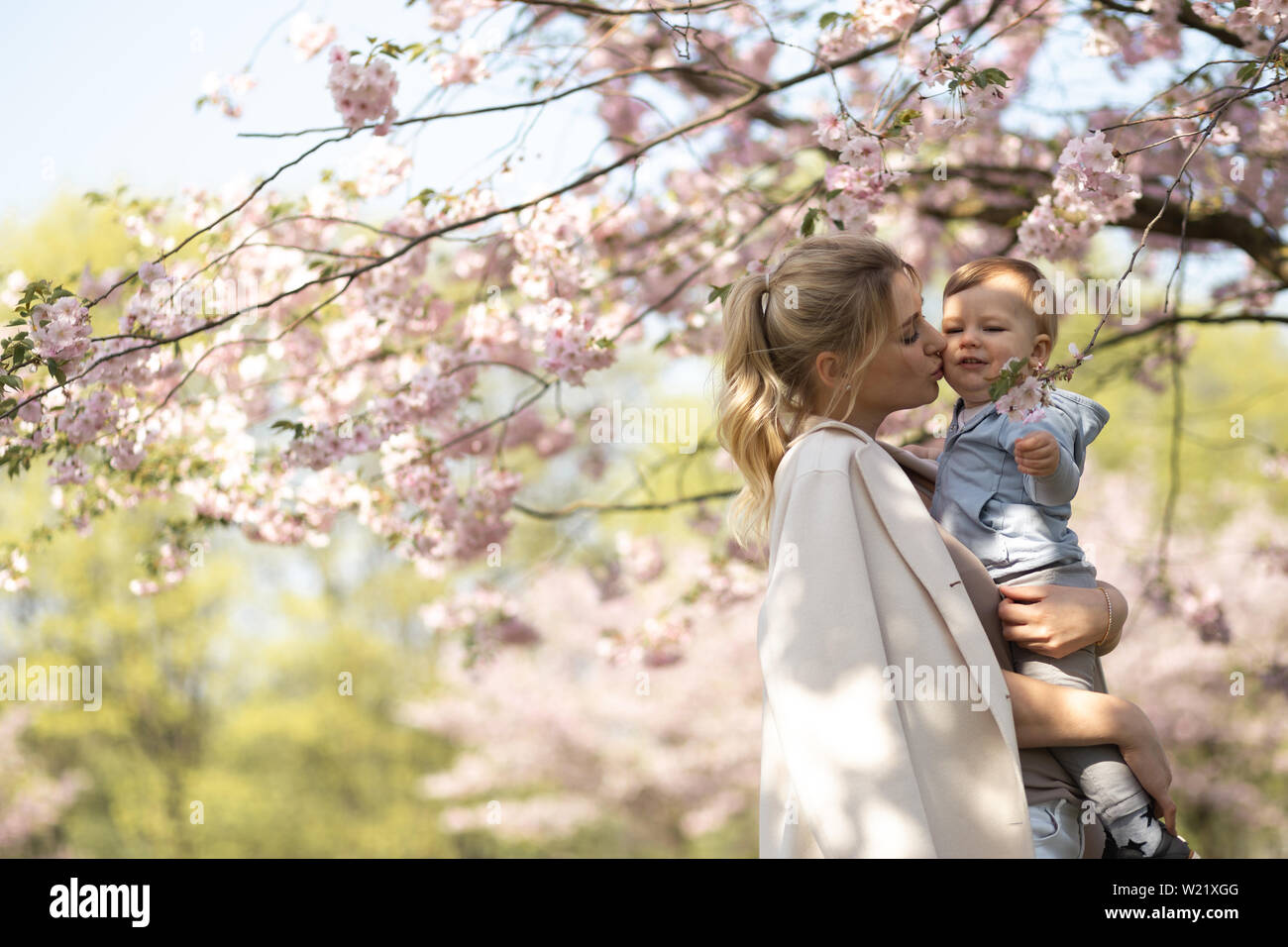 Young mother mom holding her little baby son boy child under blossoming ...