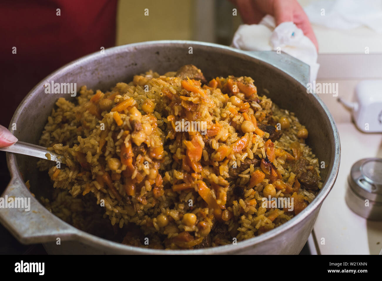 Cooking oriental pilaf in the kitchen in the cauldron. A woman prepares ...