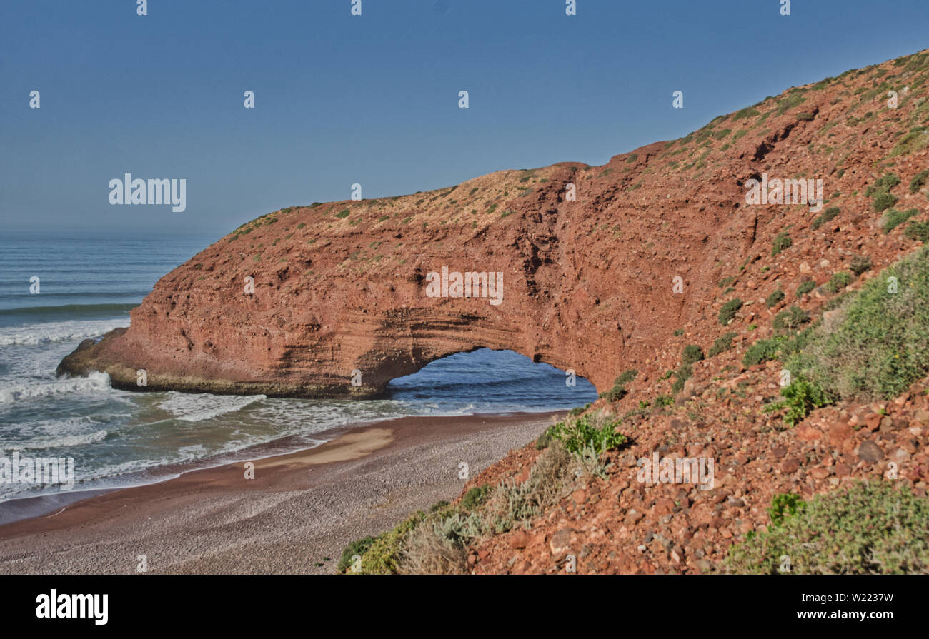 Red rock formation with arch on the beach, Plage Sidi Ifni, Morocco ...