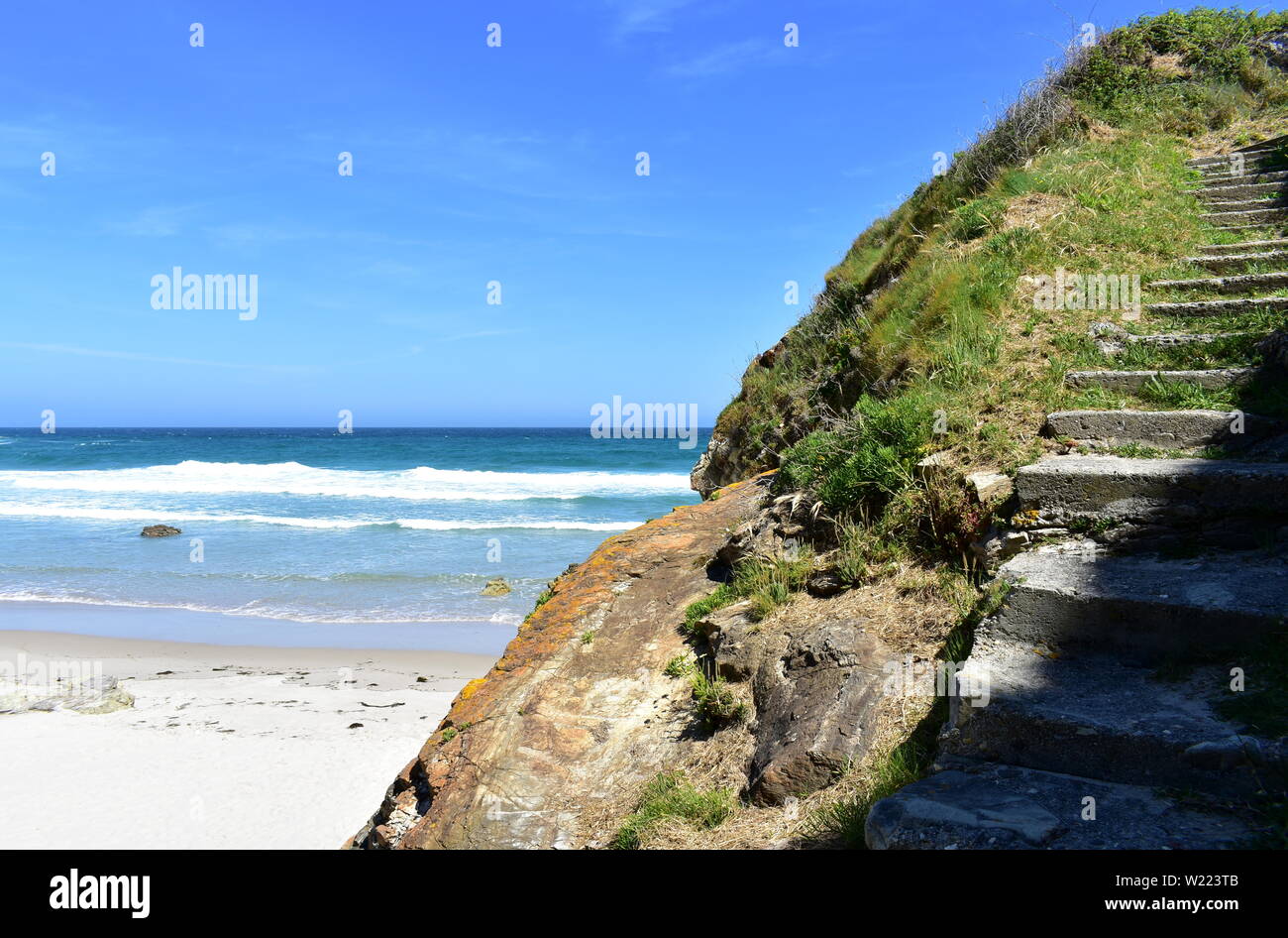 Beach with cliff, white sand, waves and stairs. Blue sky, sunny day ...