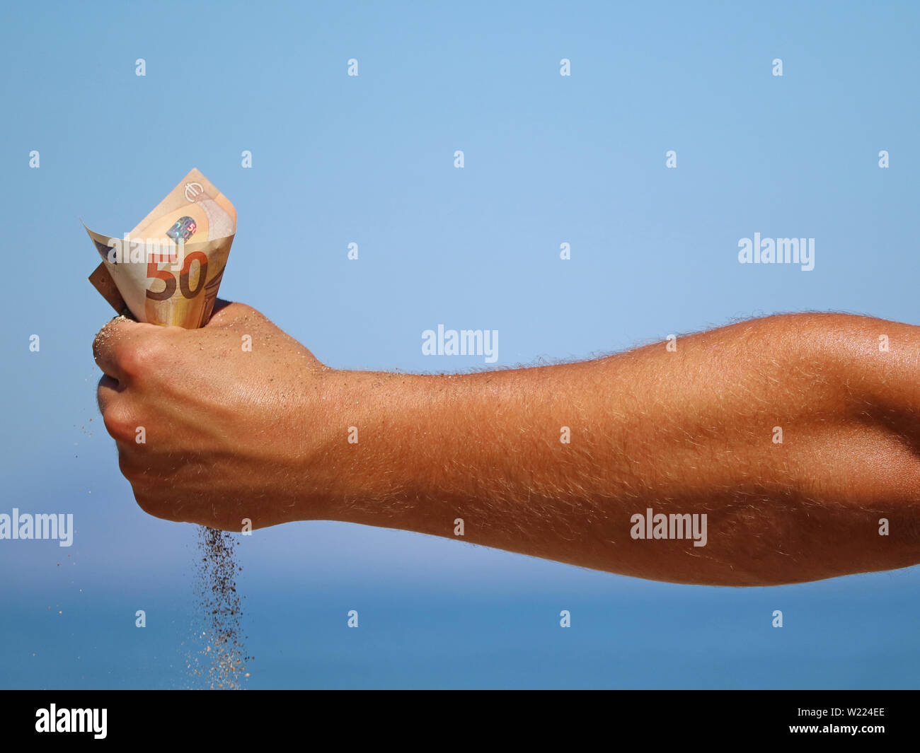 male arm holds fifty euro banknote and lets sand trickle through on ...
