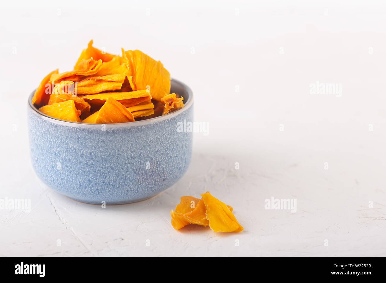 Mango chips in a blue bowl and pieces of this fruits on a table ...