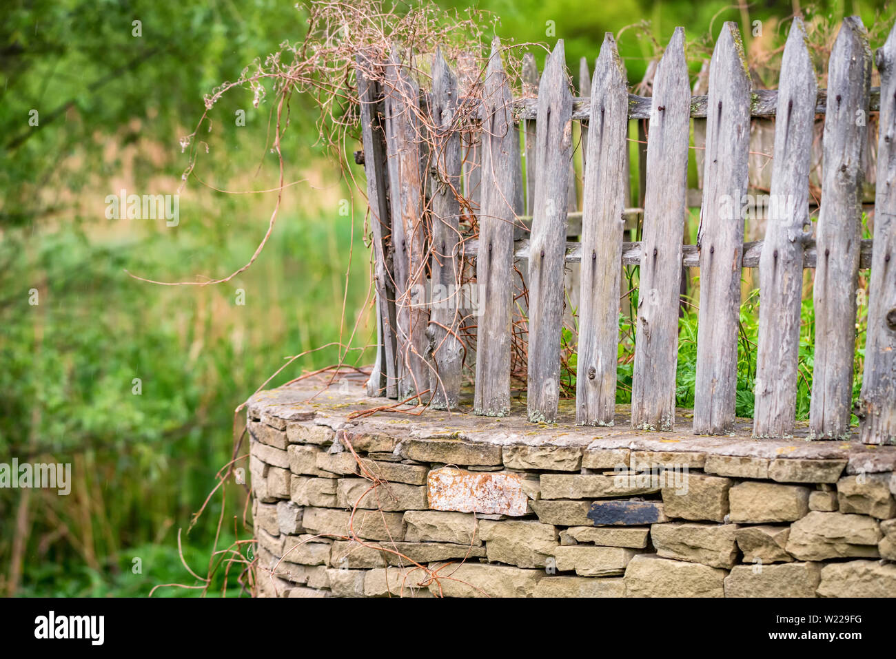 View of rural fence made of stones and wooden planks and green grass ...