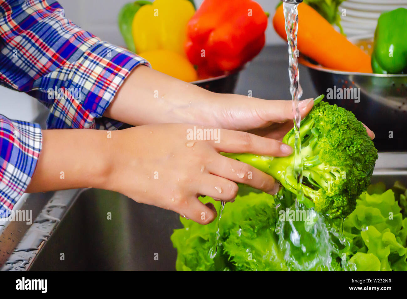 Young woman washing broccoli to remove pesticides before cooking in ...