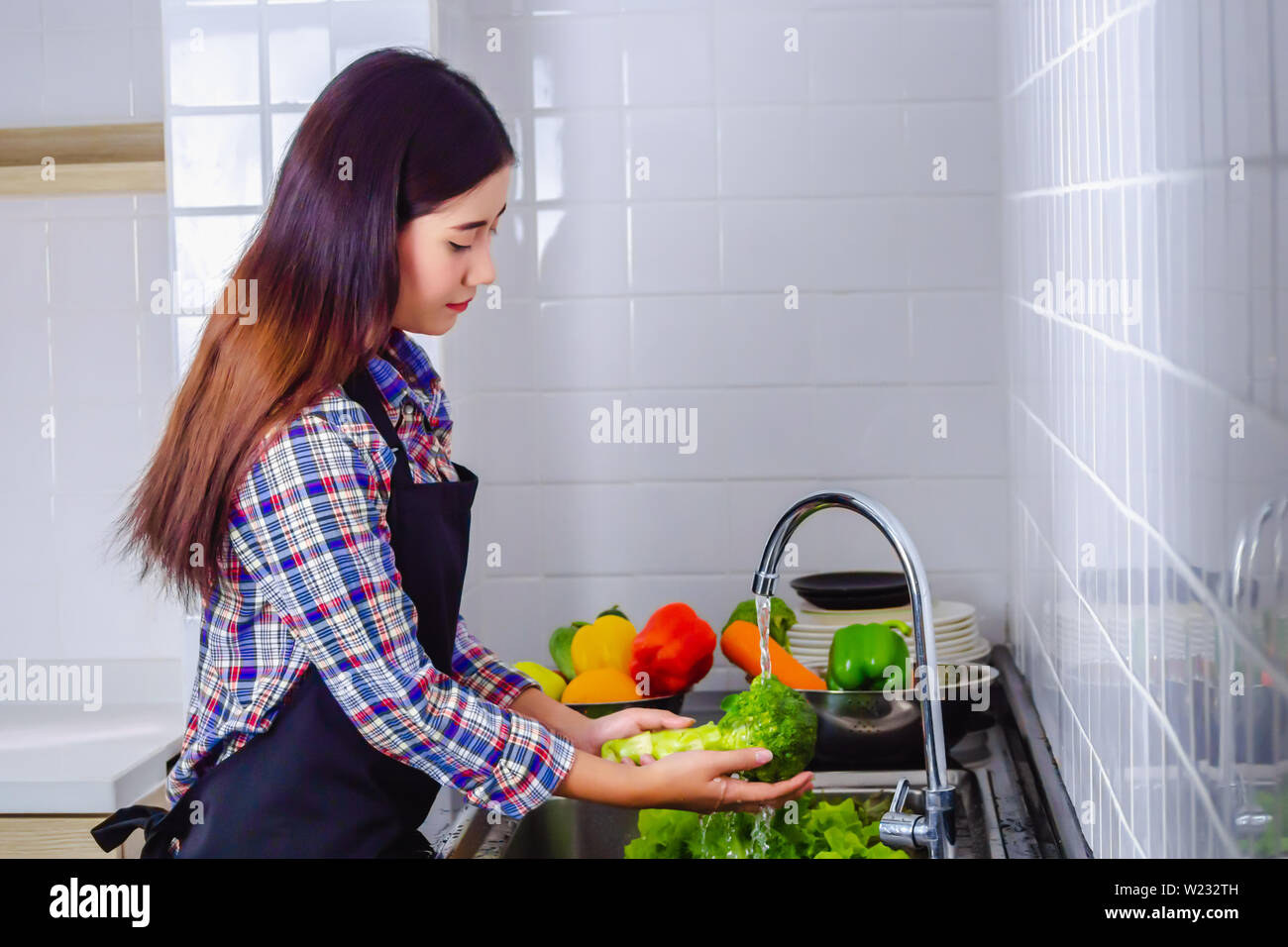 Young woman washing carrot to remove pesticides before cooking in ...