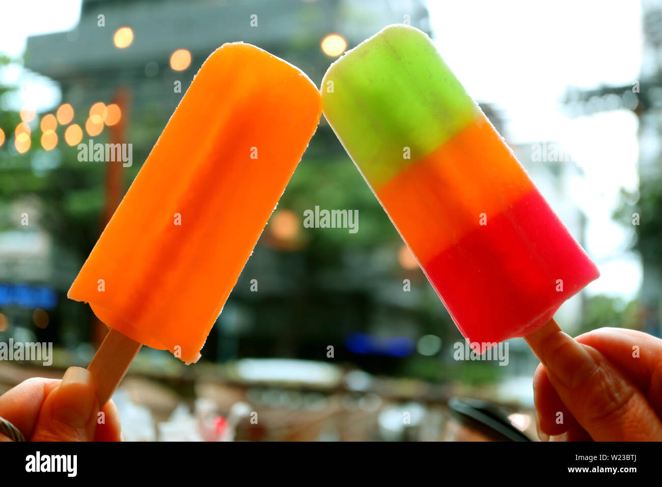 Clinking with two mix colorful popsicles against blurry urban evening ...